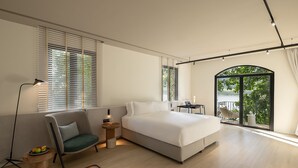 Quarto moderno com cama, uma cadeira, escrivaninha e vista para o exterior.