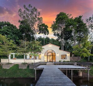 Uma casa com uma grande entrada em arco, um deck de madeira e um lago na frente.