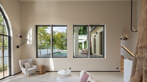 Um interior moderno com janelas amplas, um sofá branco, uma mesa redonda de madeira e uma escadaria.