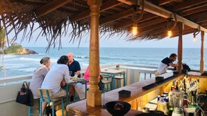 Um restaurante à beira-mar com mesas e cadeiras de madeira, um espaço de bar e vista para o oceano.