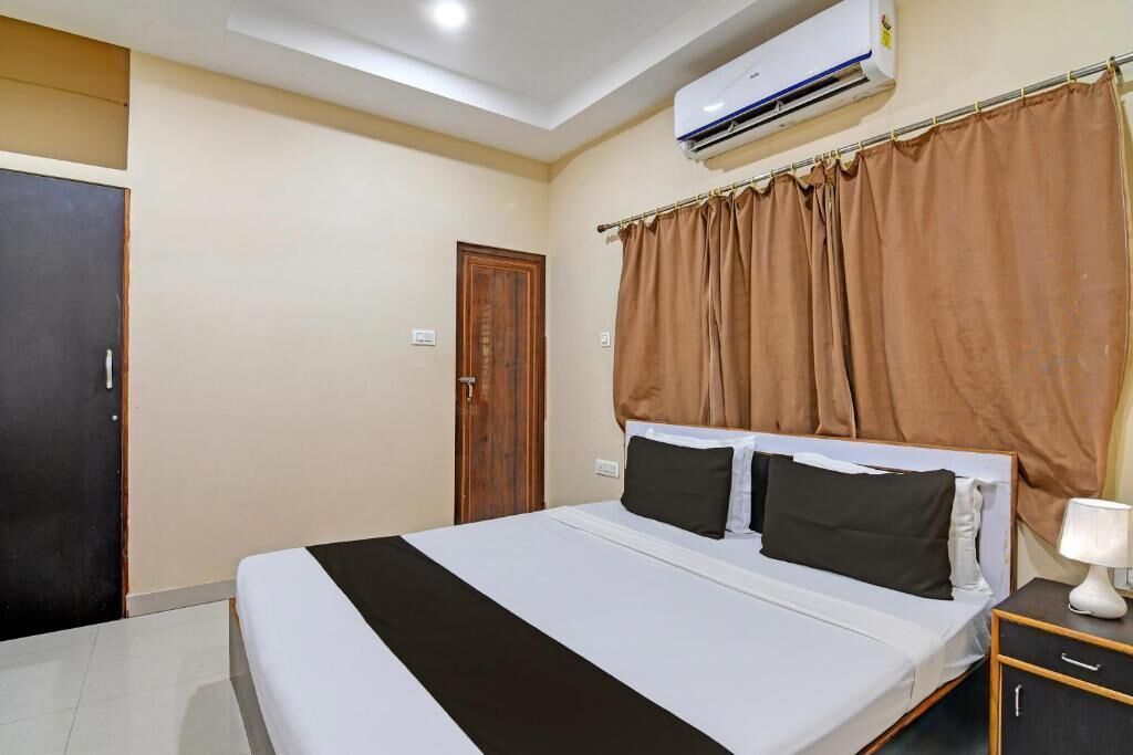 Quarto de hotel com cama, mesa de cabeceira, ar condicionado, porta e cortinas.