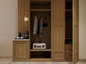 Um guarda-roupa de madeira com prateleira embutida, cabideiro e uma pequena mesa com cafeteira e chávenas.