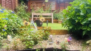 Um jardim com um banco de madeira, diversas plantas e estátuas.