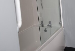 Uma casa de banho com cabine de duche em vidro, uma banheira branca e chuveiro visível.