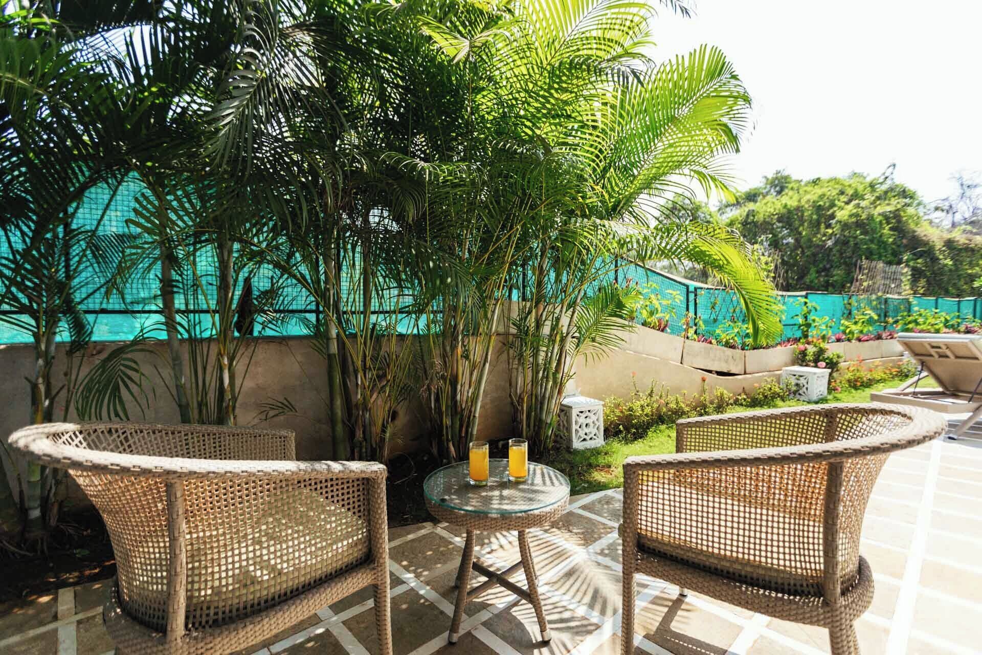 Uma área de pátio com cadeiras de vime, uma mesa de vidro e vista para uma piscina e vegetação.