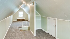Um quarto com teto inclinado, janela, banco embutido e porta.
