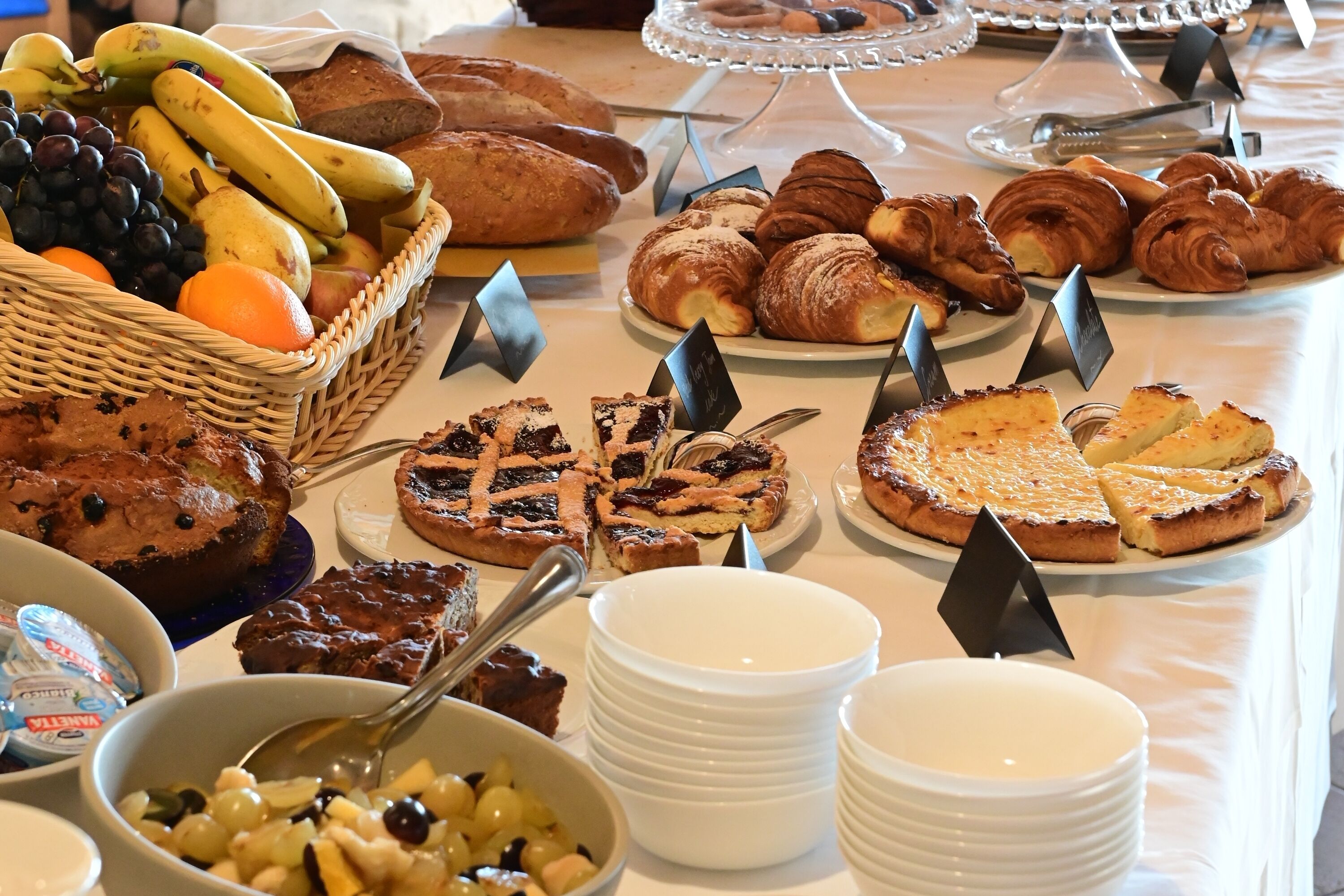 Uma mesa de buffet com diversos produtos de panificação, incluindo tortas, doces e pão.