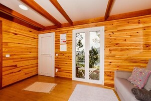 Um quarto com painéis de madeira e uma porta de vidro deslizante para uma área externa, um sofá com almofadas e um pequeno tapete no chão.