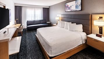 Quarto de hotel com uma cama grande, uma escrivaninha, um sofá e uma televisão.