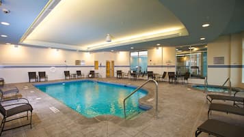 Uma piscina interior com espreguiçadeiras e mesas, uma cadeira de salva-vidas e um aviso de proibição de mergulho.