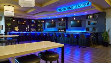 Uma área de bar com uma placa que diz 'PHOTO FINISH LOUNGE', banquetas, balcão de bar e uma televisão na parede.