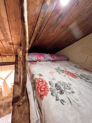 Um quarto com teto de madeira, colcha florida e parede de tijolos.