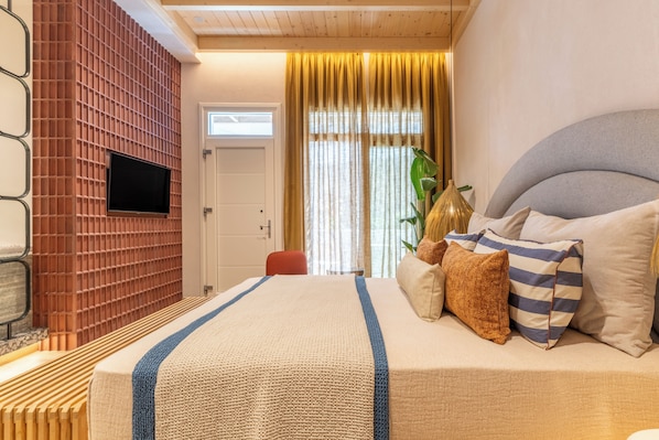 Quarto de hotel com cama, televisão na parede, janela com cortinas e uma planta.