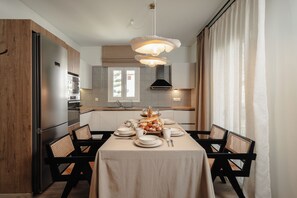 Cozinha moderna com mesa de jantar posta para quatro pessoas, exibindo frutas em destaque, cadeiras de madeira e luminária pendente.