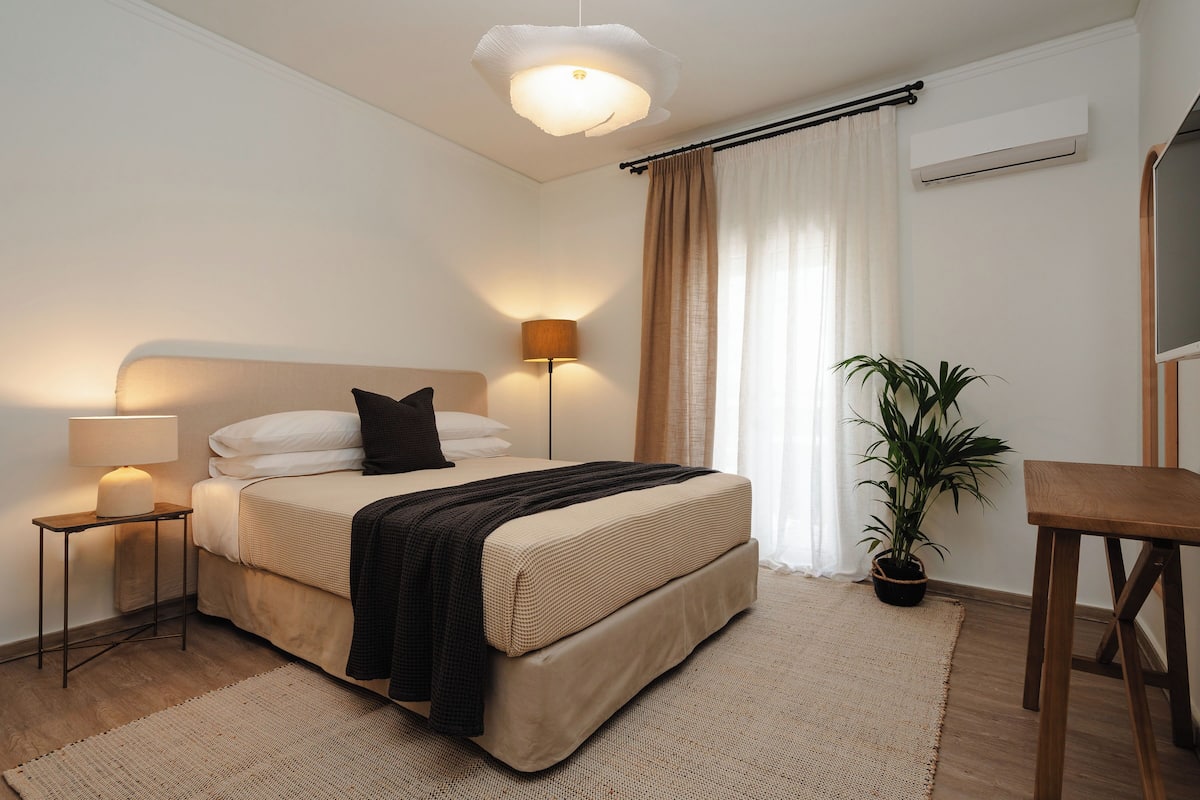 Quarto bem arrumado com cama, abajures, planta em vaso e cadeira de madeira.