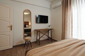 Quarto de hotel com cama, televisão na parede, secretária de madeira, espelho e porta.