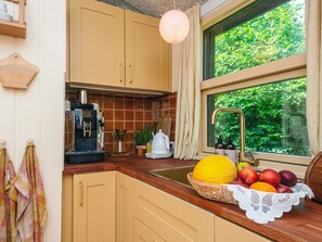 Cozinha com armários de madeira, cafeteira, chaleira e uma cesta de frutas no balcão.