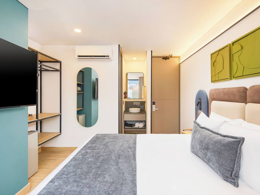 Quarto de hotel moderno com cama, televisão, armário e banheiro.