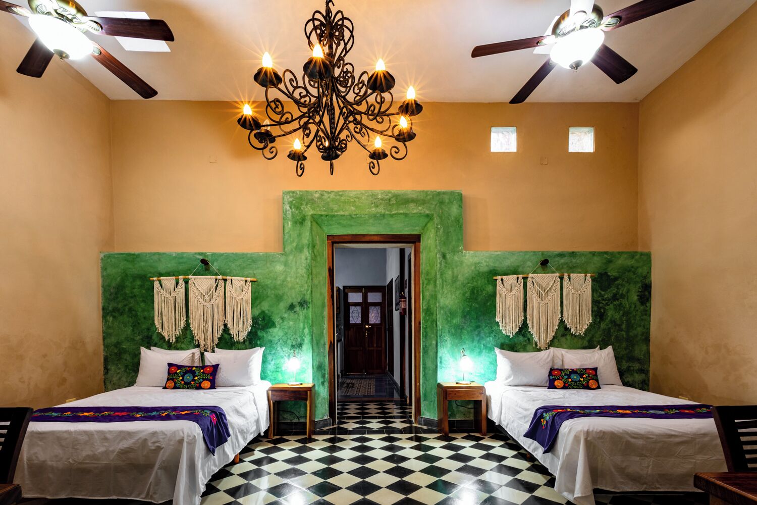 Quarto com duas camas, um lustre, ventiladores de teto e piso xadrez.