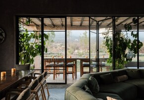 Um interior moderno com área de jantar, sofá e grandes janelas com vista para o exterior.
