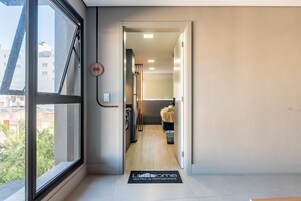 Quarto de hotel com uma janela grande, uma porta com placa de identificação, um tapete de entrada e vista para o exterior.