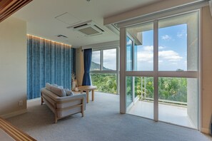 Quarto moderno com sofá, uma mesinha e grandes janelas com vista para áreas verdes e montanhas.