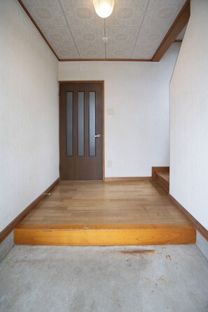 Um corredor com piso de madeira, uma porta com painéis verticais e teto estampado.