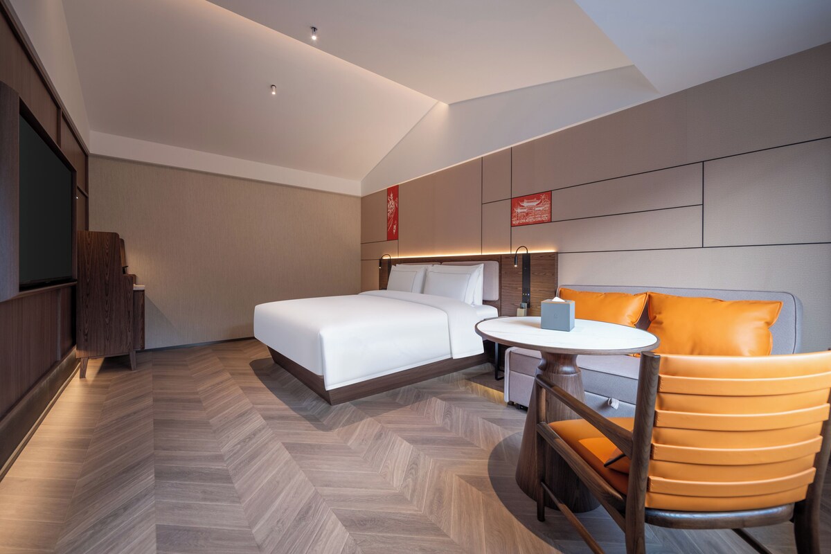Quarto de hotel moderno com uma cama, uma mesa redonda e uma cadeira.