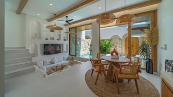 Uma sala de estar moderna com televisão, sofá, mesa de jantar, cadeiras e escada.