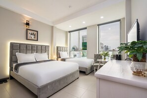 Quarto de hotel com uma cama grande, uma cama menor, uma escrivaninha e vista para a cidade.