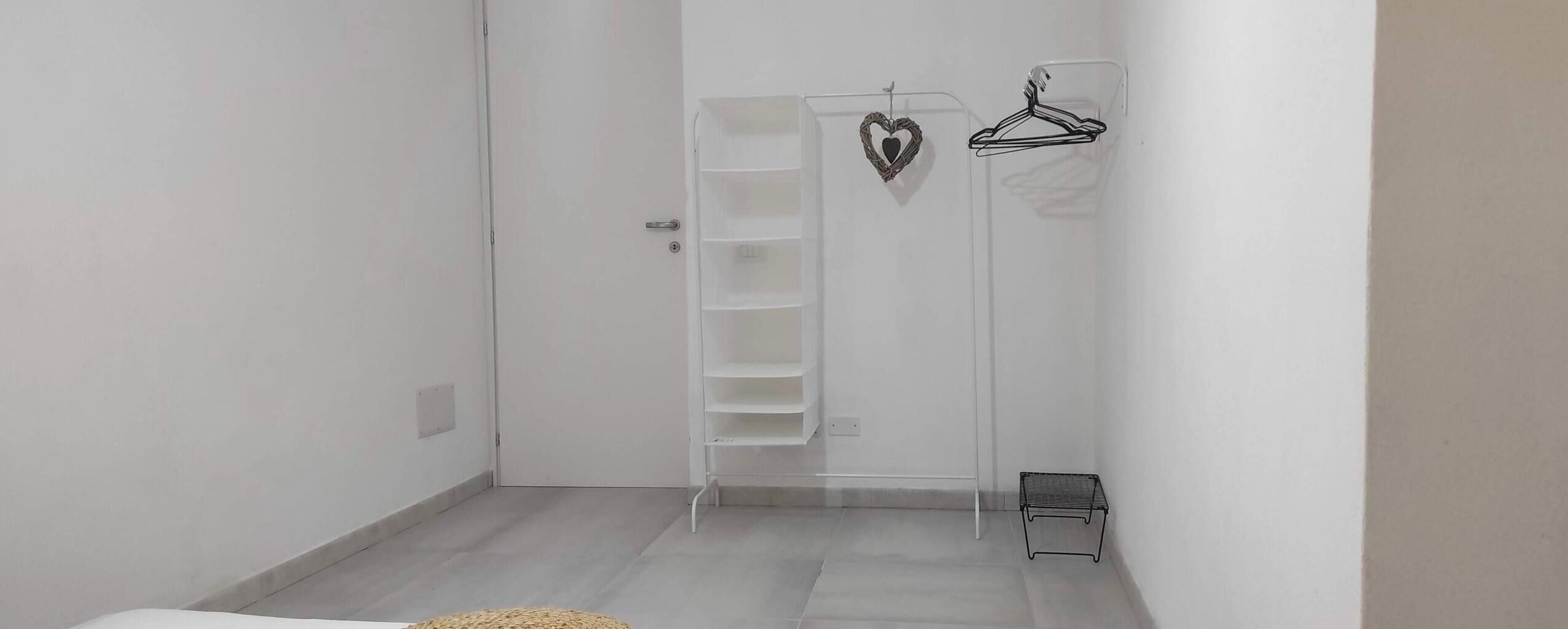 Um corredor com uma porta branca, um armário branco com barra para pendurar roupas e uma pequena estante.