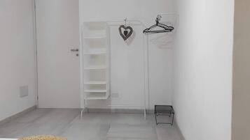 Um corredor com uma porta branca, um armário branco com barra para pendurar roupas e uma pequena estante.