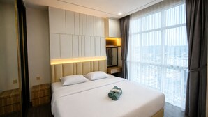 Quarto de hotel com uma cama, mesa de cabeceira, espelho, janela com cortinas e vista para a cidade.