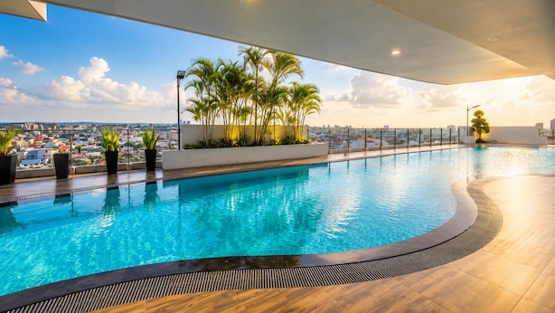 Piscina infinita no terraço com vista para a cidade, rodeada por vasos de plantas e palmeiras.