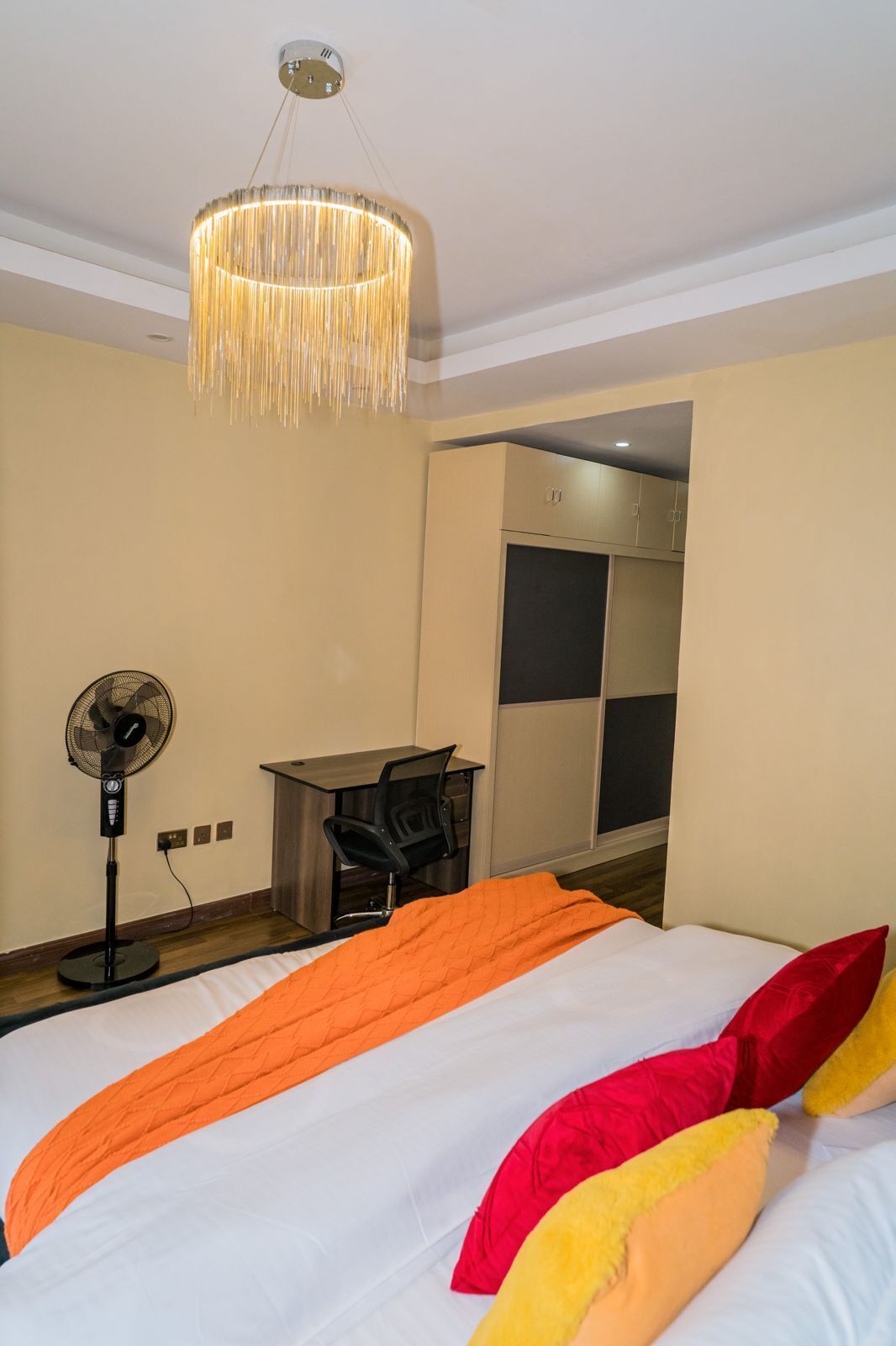 Quarto de hotel com cama, escrivaninha, cadeira, ventoinha e espelho.