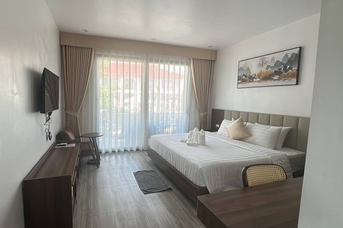 Quarto de hotel com cama, escrivaninha, cadeira, televisão e janela com cortinas.