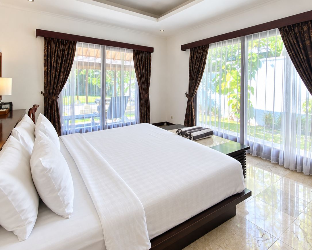 Quarto de hotel com uma cama grande, uma escrivaninha e vista para o exterior através de amplas janelas.