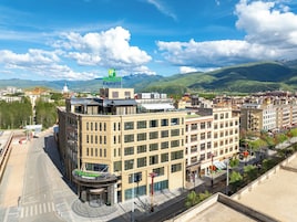 Um hotel com uma placa de destaque, rodeado por edifícios urbanos e montanhas ao fundo.