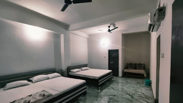 Quarto com duas camas, um ventilador de teto, um banco e uma porta.
