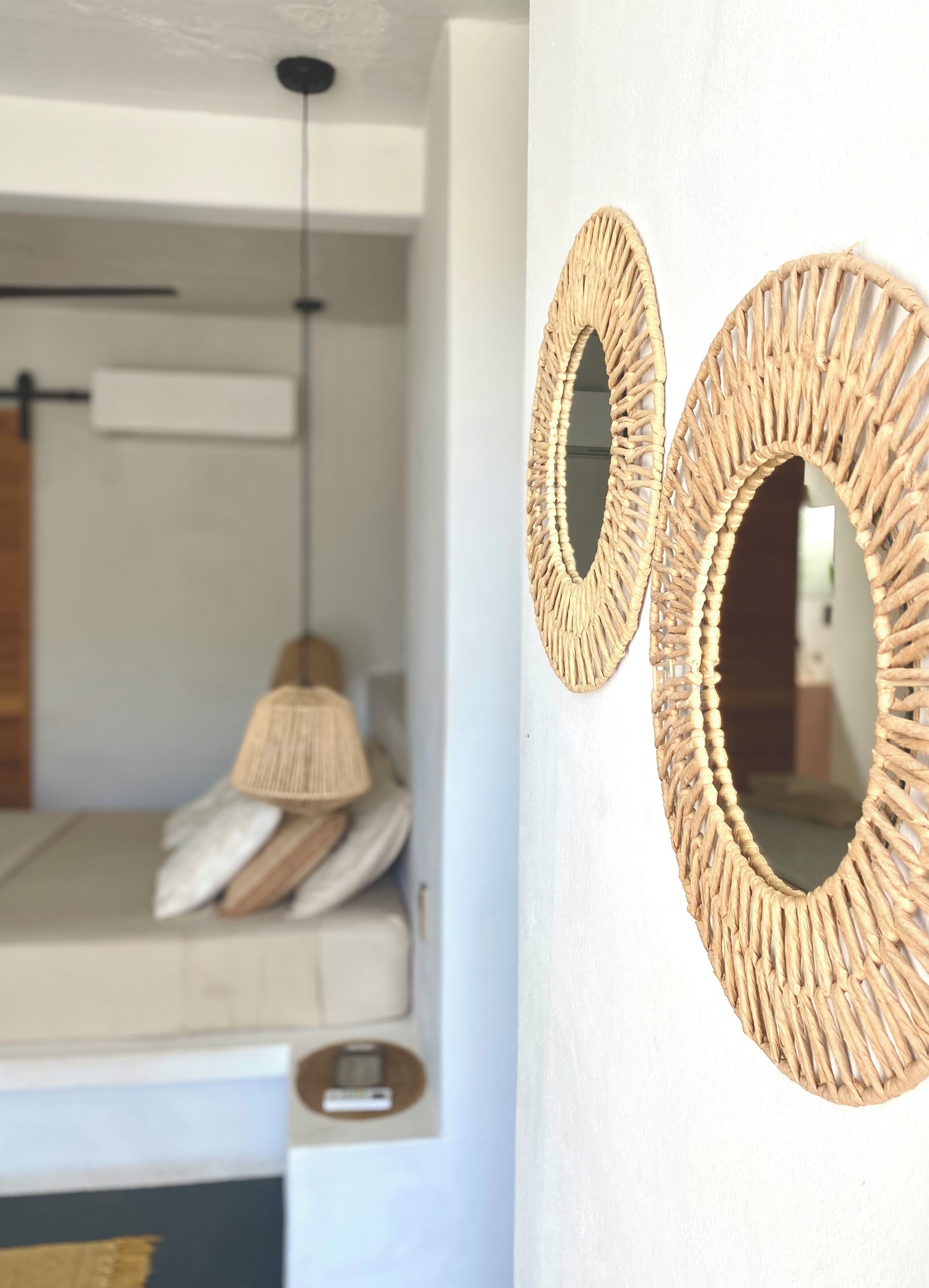 Quarto com cama, luminária pendente e dois espelhos de parede em tear.