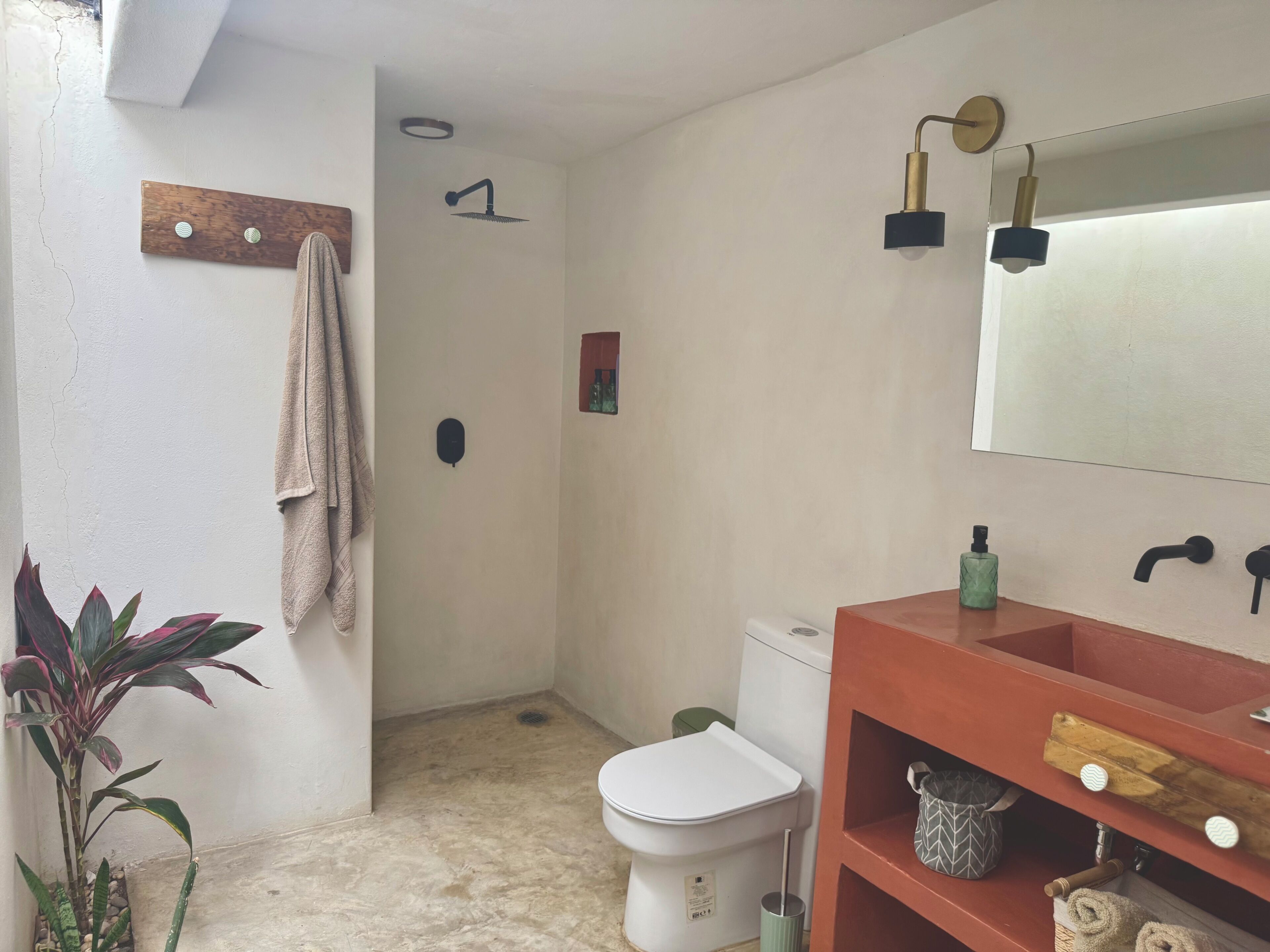 Uma casa de banho com sanita, chuveiro, lavatório e barra de toalhas.