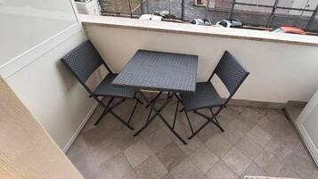 Uma varanda com mesa e cadeiras, vista para a rua e piso de azulejos.