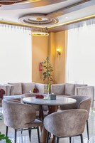 Uma sala de jantar moderna com uma mesa redonda, assentos acolchoados, um lustre e uma planta.