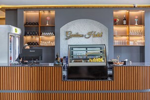 Uma área de recepção de hotel com arco de mármore, balcão com vitrine e prateleiras com copos e objetos decorativos.