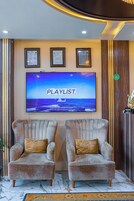 Um quarto com duas poltronas, uma televisão de tela grande exibindo 'PLAYLIST' e certificados emoldurados na parede.