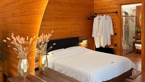 Quarto de madeira com cama, mesas de cabeceira, um porta-toalhas e área de chuveiro.