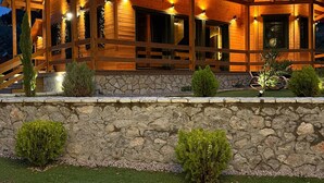 Uma cabana de madeira com base de pedra, um pátio de pedra e montanhas ao fundo.