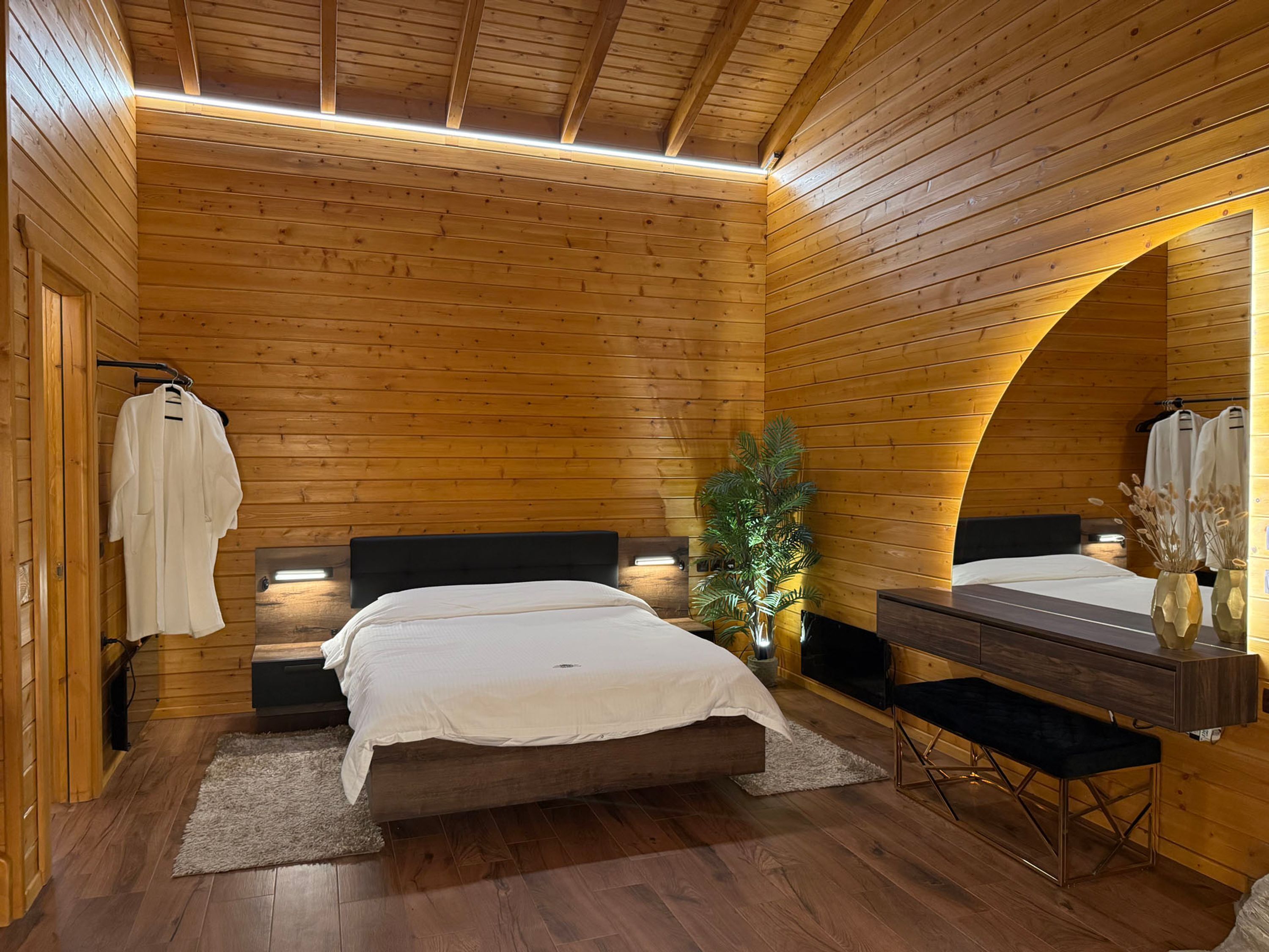 Quarto estilo cabana de madeira com cama, mesas de cabeceira, um banco e um espelho.