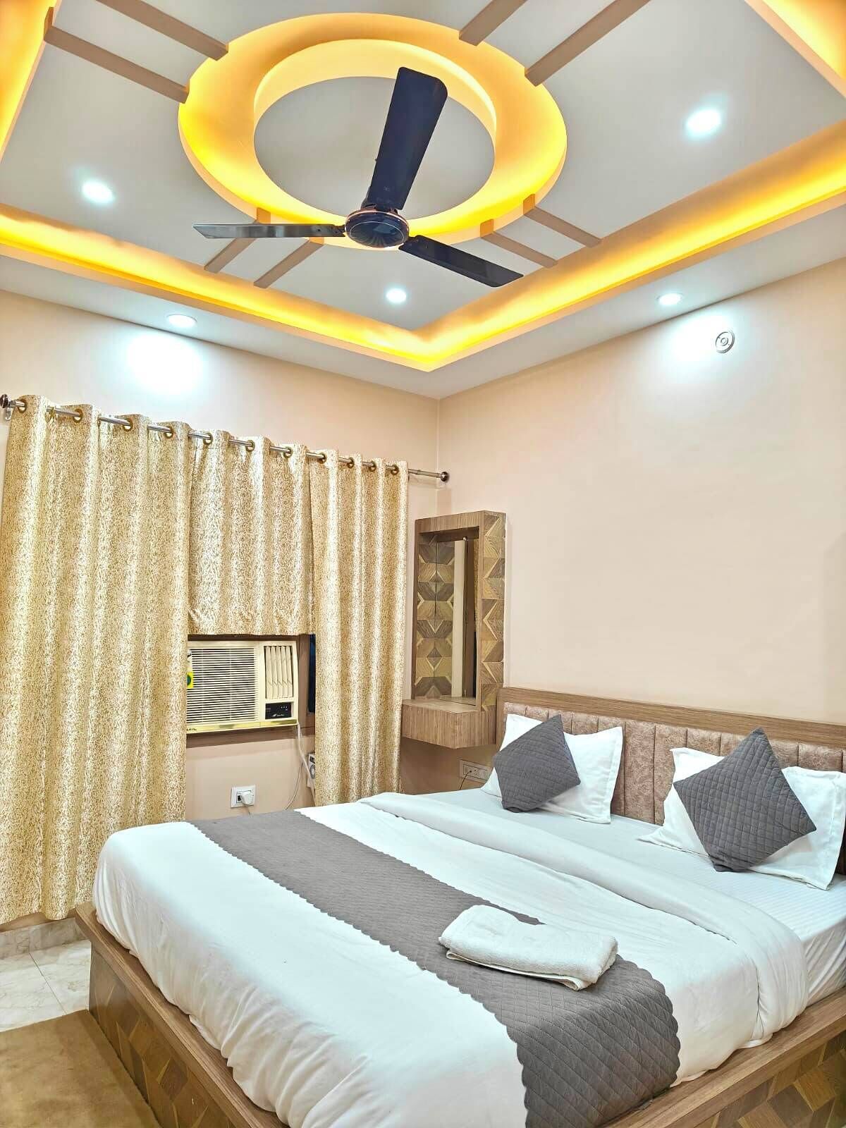 Quarto com cama, cortinas, ventoinha no teto e janela.