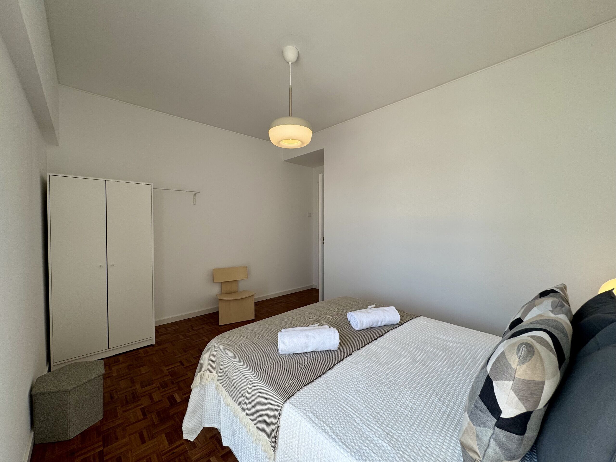 Quarto com cama, guarda-roupa, mesa de cabeceira e luminária pendente.